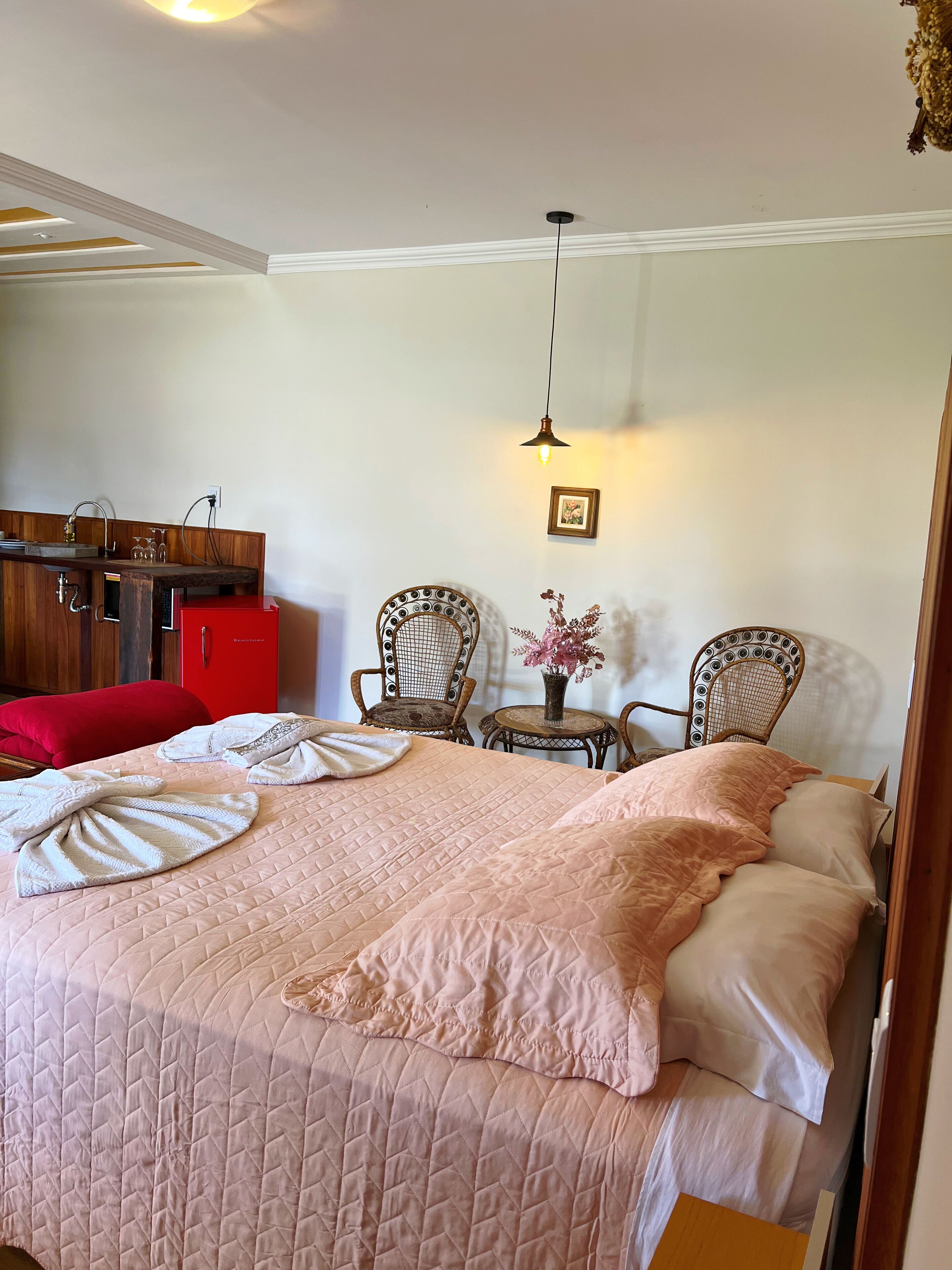 Quarto com uma cama, duas cadeiras, uma mesinha e um armário vermelho.