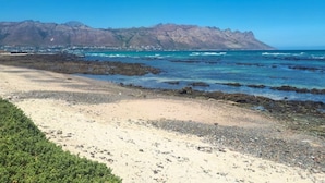 Uma praia com costa rochosa, água azul límpida e montanhas ao longe.