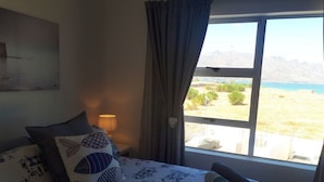 Quarto com cama, almofadas, luminária e janela com vista para a paisagem.