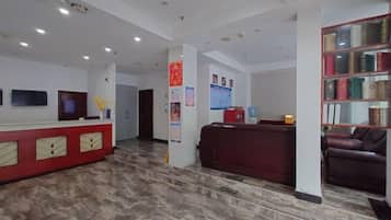 Um saguão de hotel com balcão de recepção, um sofá, uma estante de livros e uma televisão.