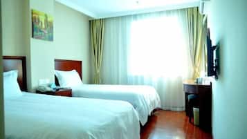 Quarto de hotel com duas camas, uma escrivaninha, uma cadeira, janela com cortinas e um quadro na parede.