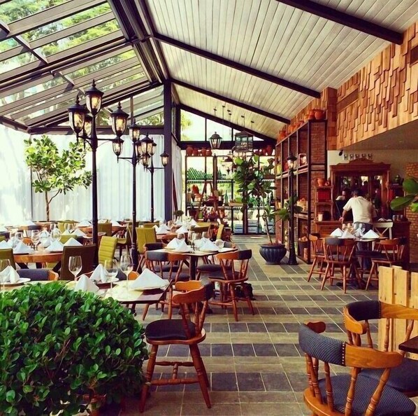 Restaurante interno com móveis de madeira, mesas preparadas para refeições e lanternas penduradas.