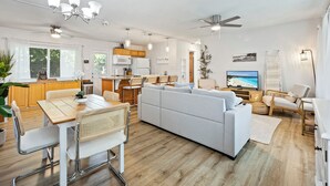 Uma sala de estar moderna com sofá, mesa de jantar e cadeiras. Há uma cozinha com armários e eletrodomésticos.