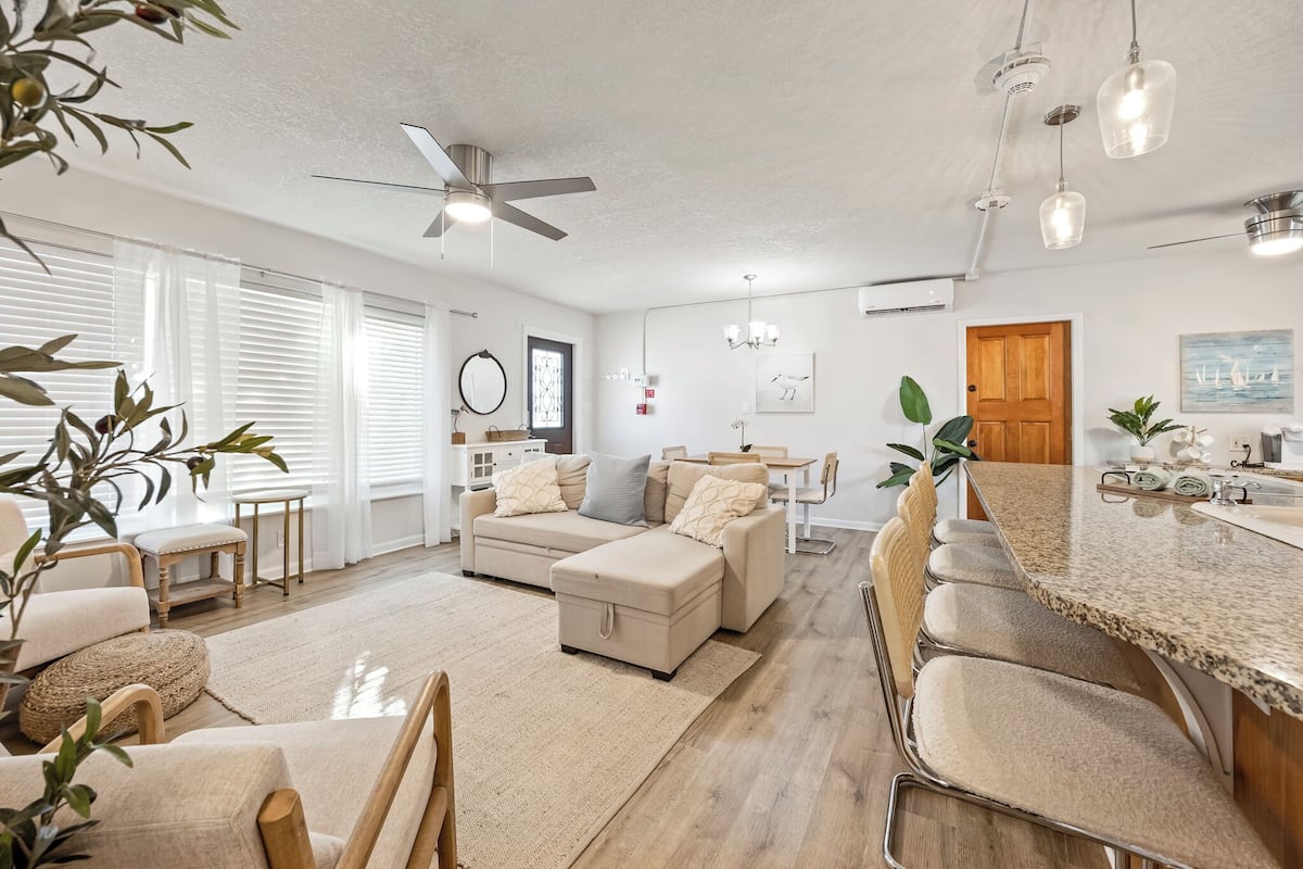 Uma sala de estar moderna com sofá seccional, área de jantar com balcão e ventoinha no teto.