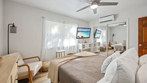 Quarto com cama, ventoinha no teto, televisão e espelho.