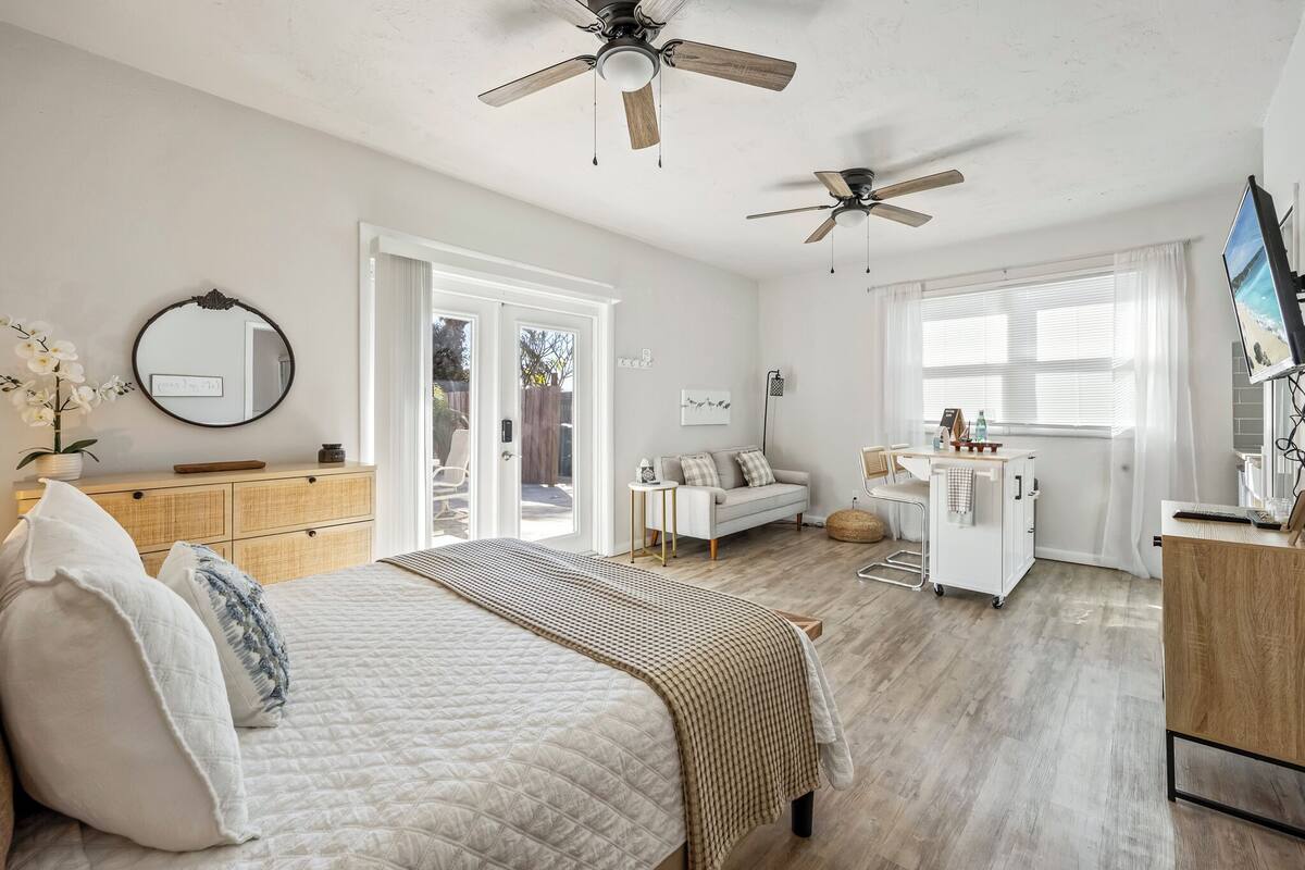 Quarto com cama, mesas de cabeceira, cômoda, espelho e ventilador de teto.