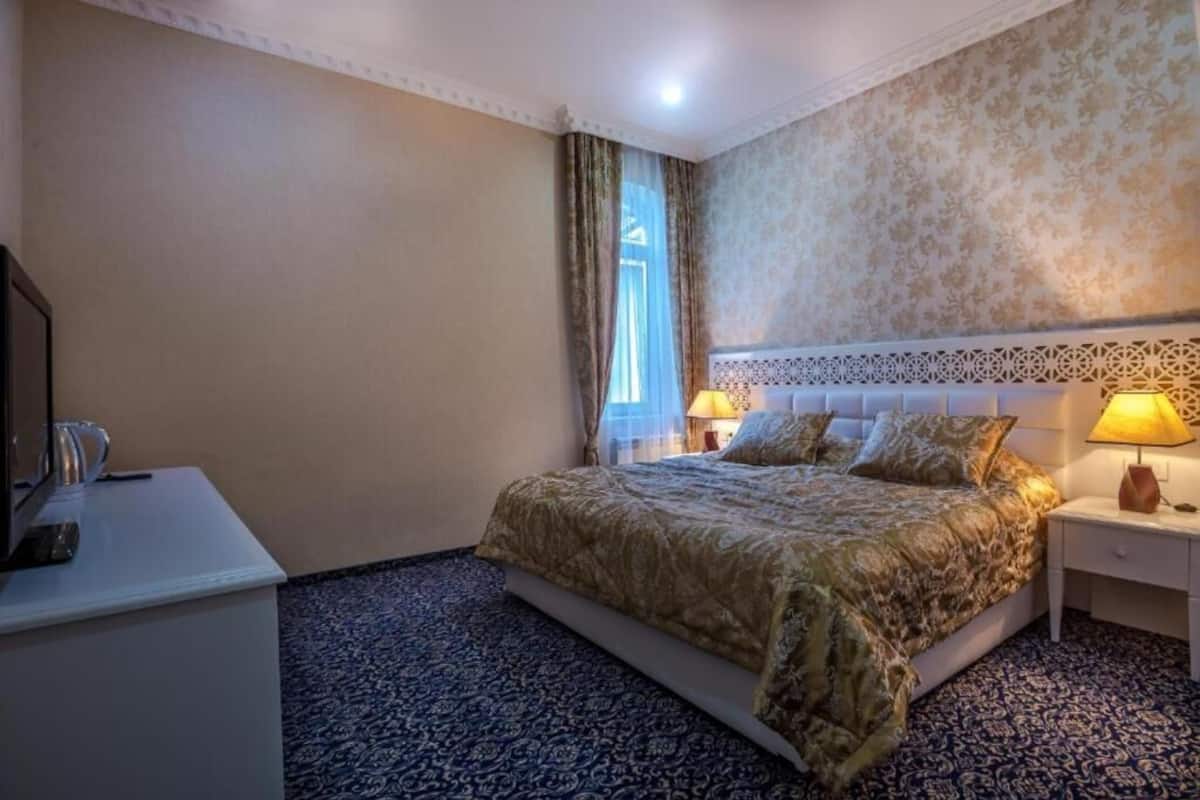 Quarto de hotel com cama, mesas de cabeceira, escrivaninha e carpete estampado.
