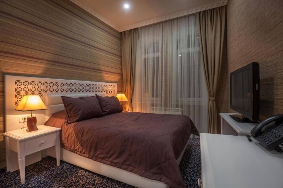 Quarto de hotel com cama, abajures, televisão e escrivaninha com telefone.