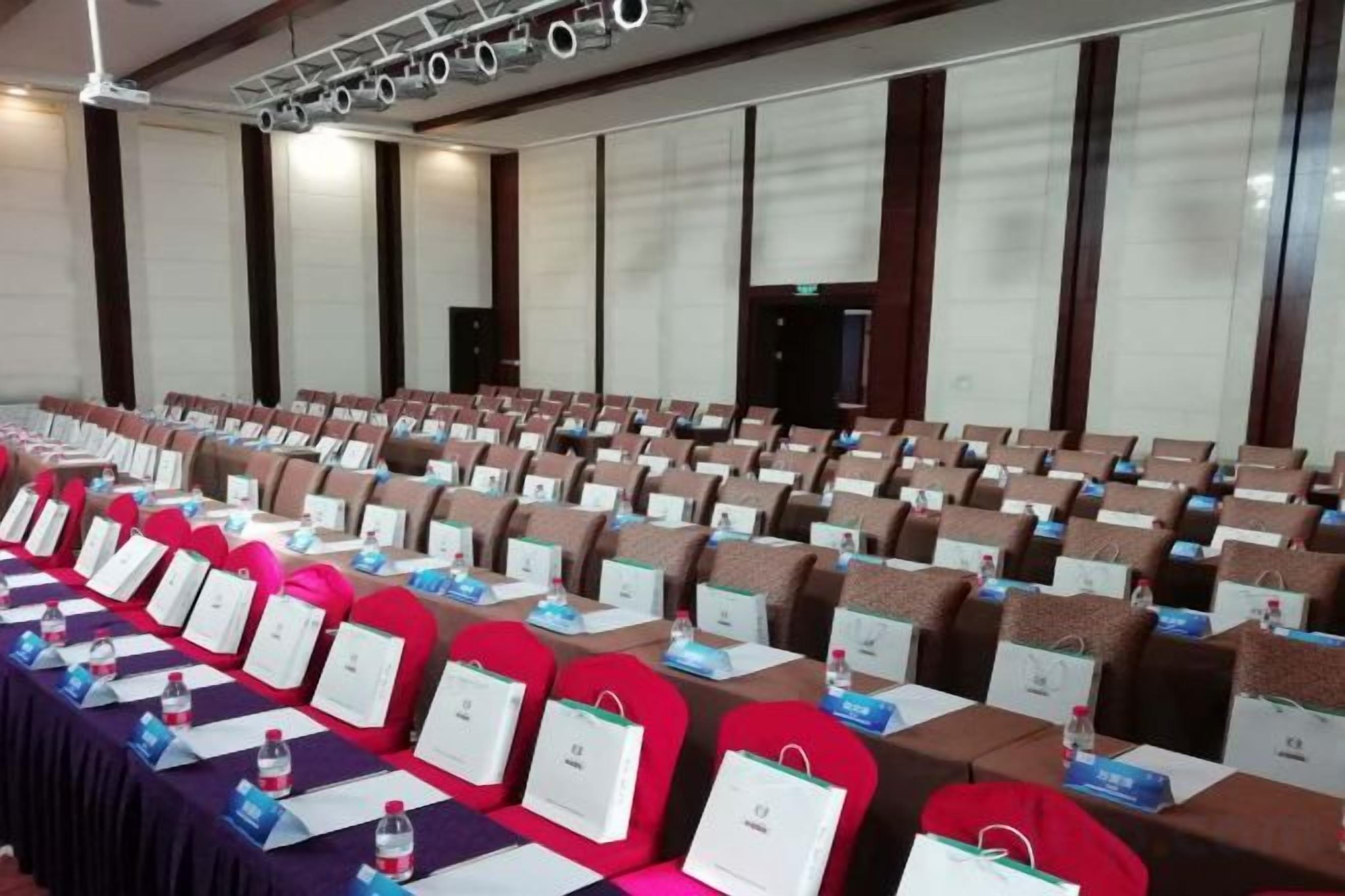 Sala de conferência com fileiras de cadeiras, placas de identificação e garrafas de água.