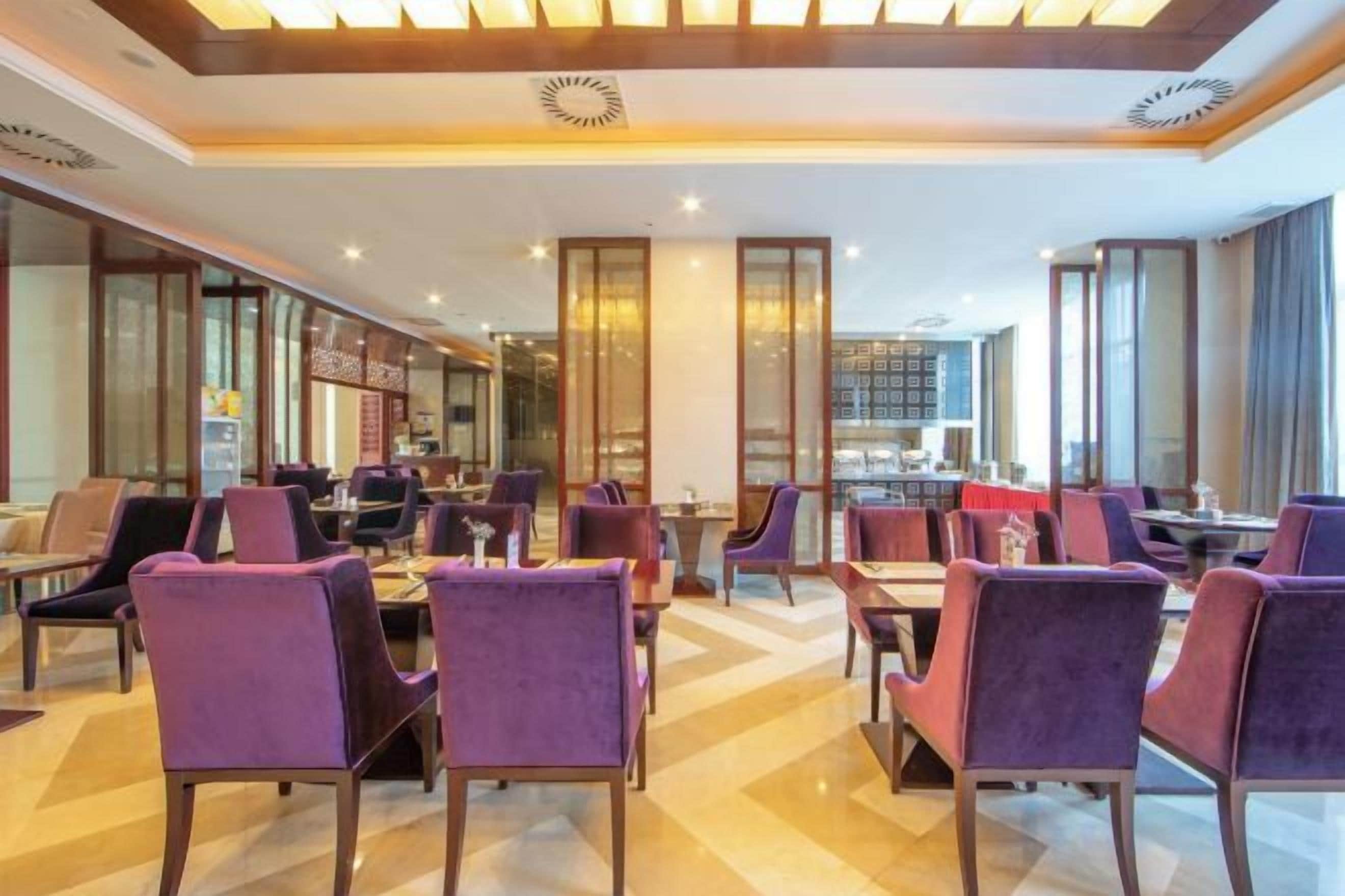 Um espaço de jantar de hotel com várias mesas e cadeiras, uma cozinha ao fundo e um design de interiores moderno.