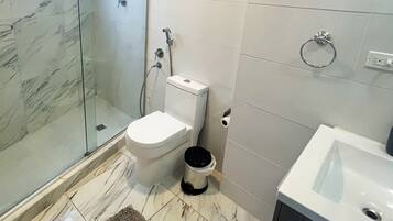 Uma casa de banho moderna com cabine de duche em vidro, sanita, bidé e lavatório.
