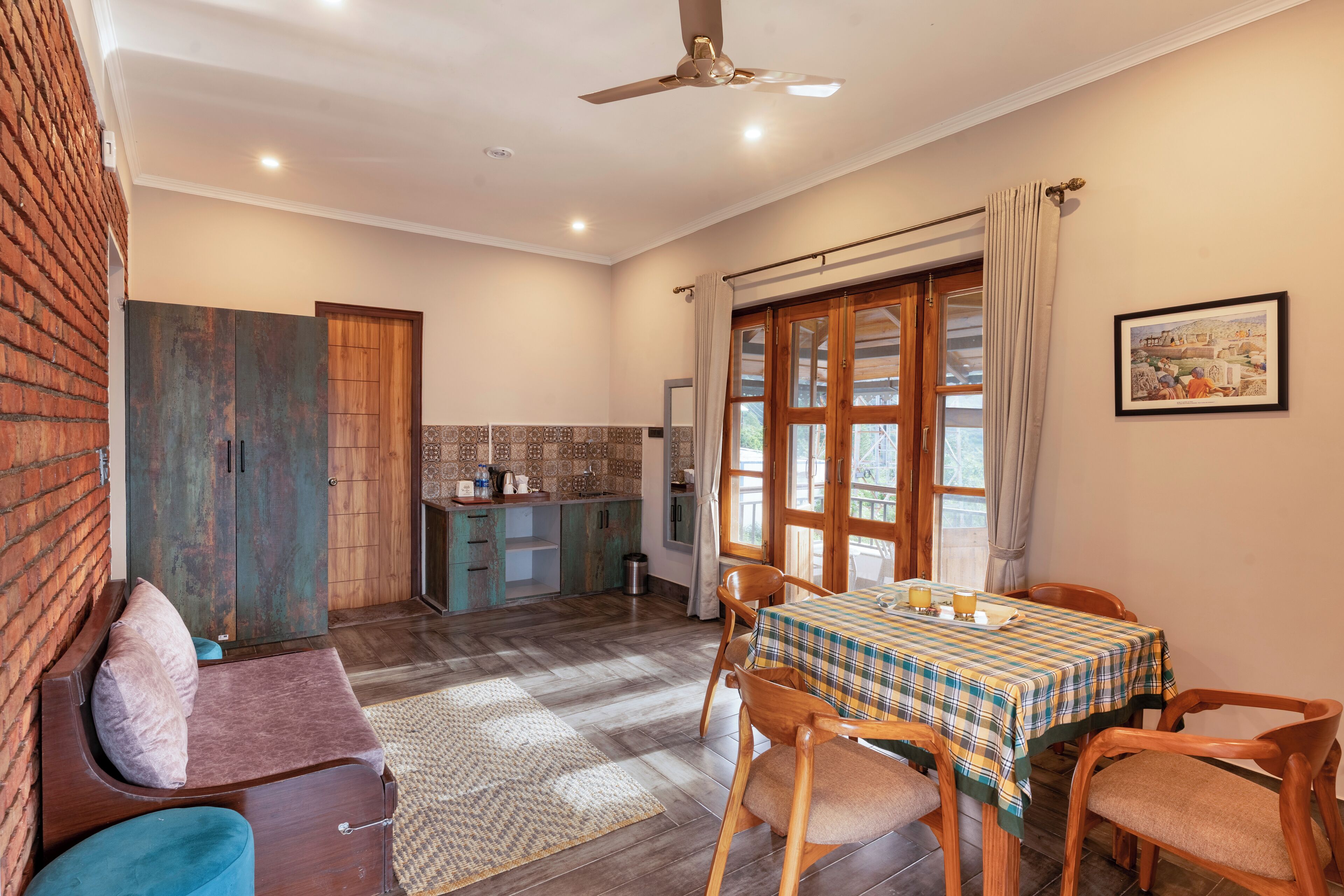 Uma sala de jantar com mesa posta para quatro pessoas, um sofá e uma cozinha ao fundo.