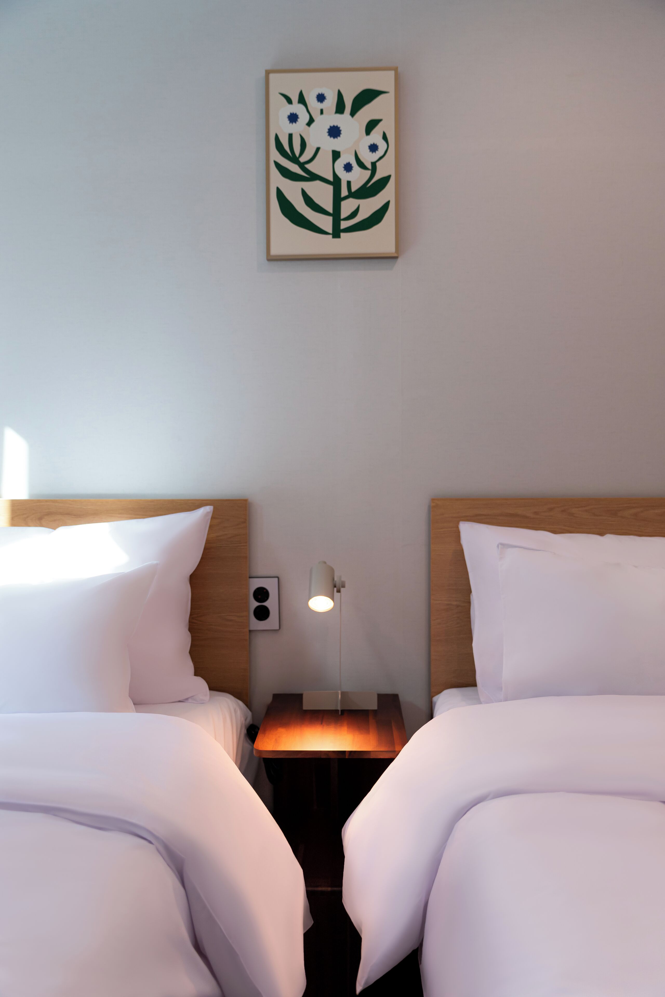 Quarto de hotel com duas camas, mesa de cabeceira com abajur e uma obra de arte pendurada na parede.
