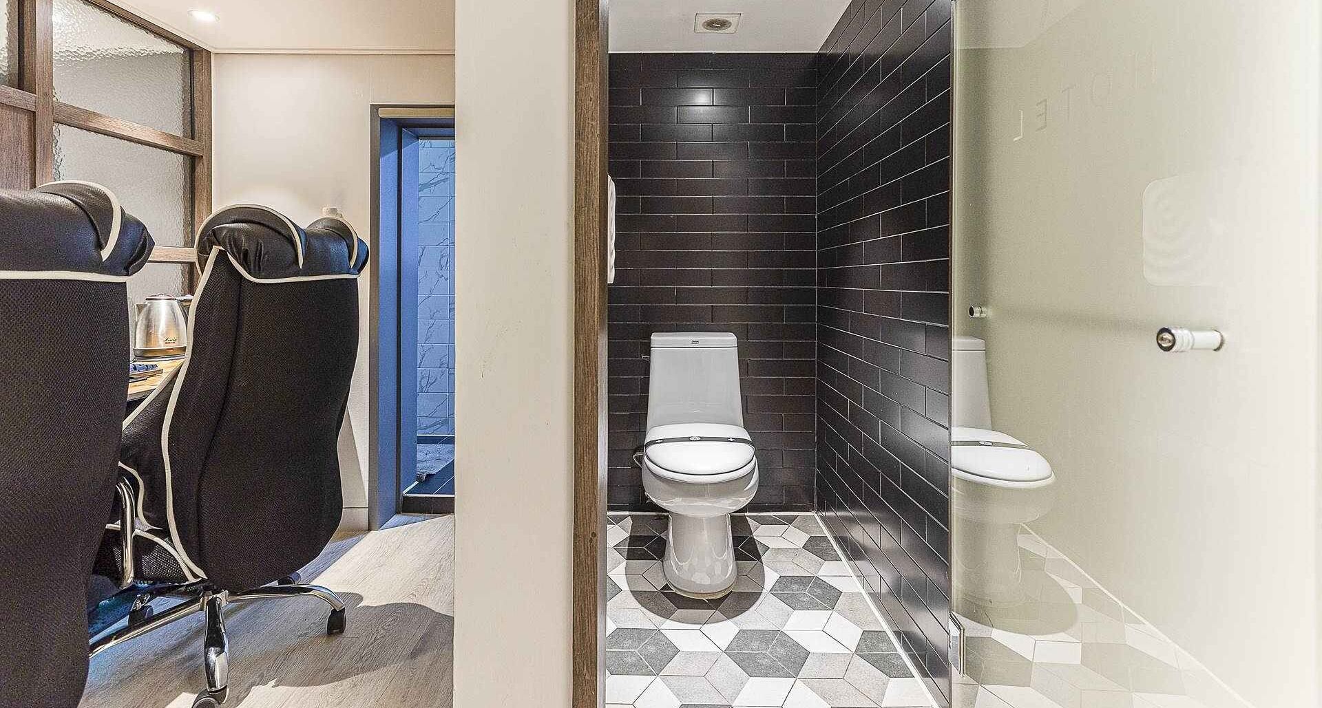 Casa de banho moderna com parede de chuveiro em mosaico preto, sanita branca e uma cadeira preta com uma toalha.