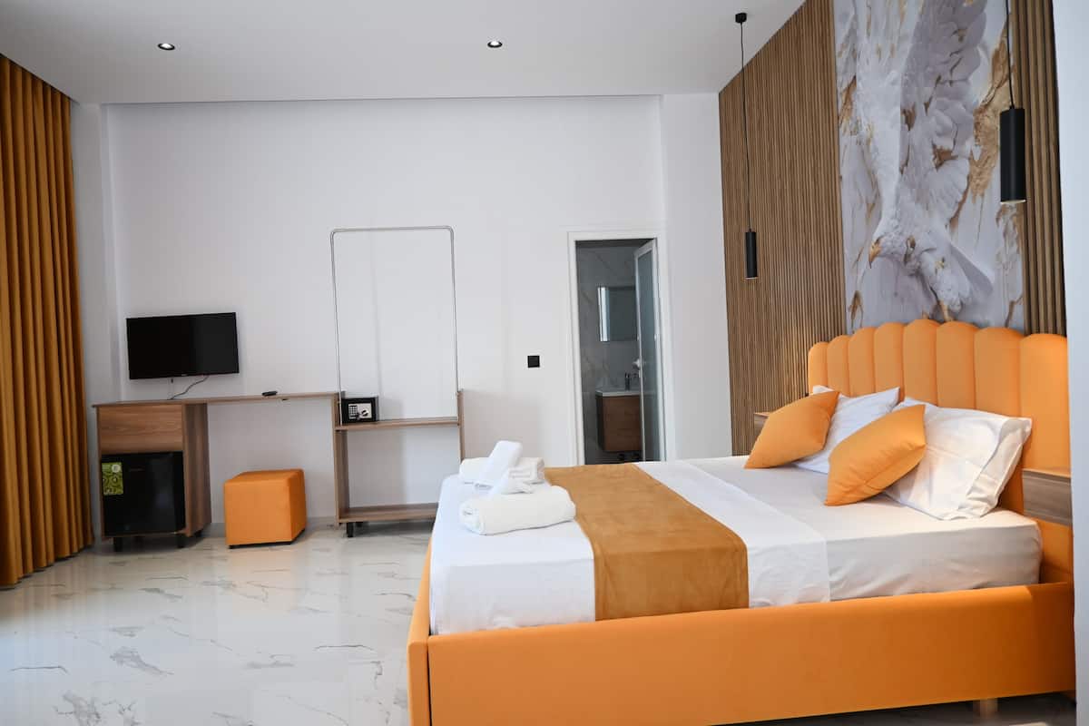 Quarto de hotel moderno com uma cama grande, uma escrivaninha, uma televisão e um guarda-roupa.