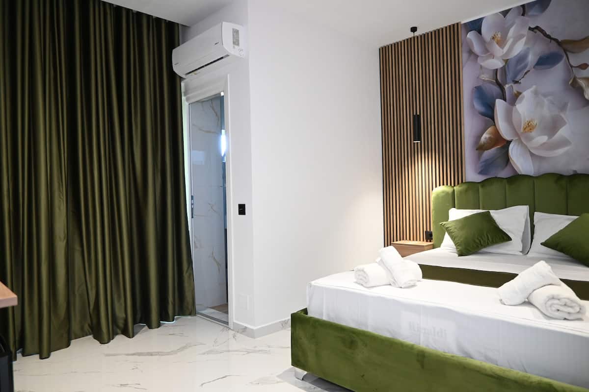 Quarto de hotel moderno com cama estofada em verde, um grande mural floral na parede e cortina verde.