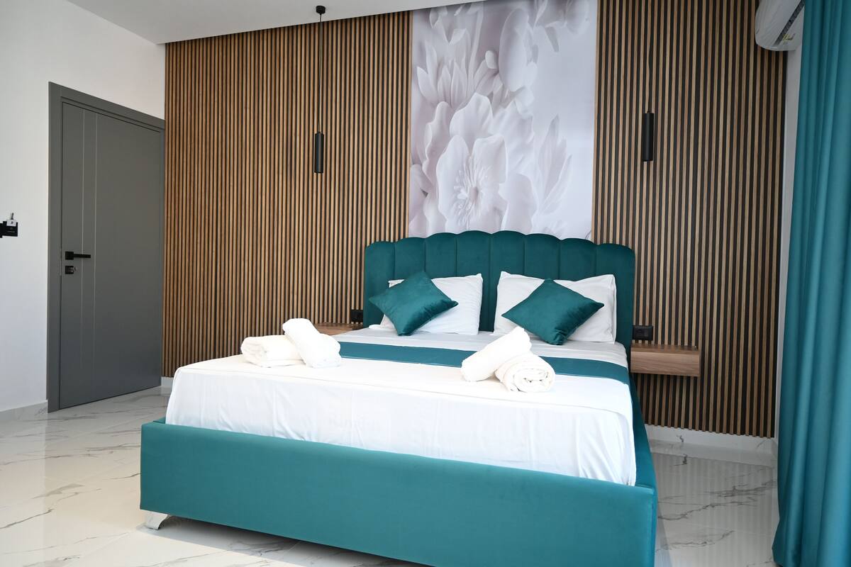 Quarto moderno com cama verde-água, roupa de cama branca e almofadas verdes.