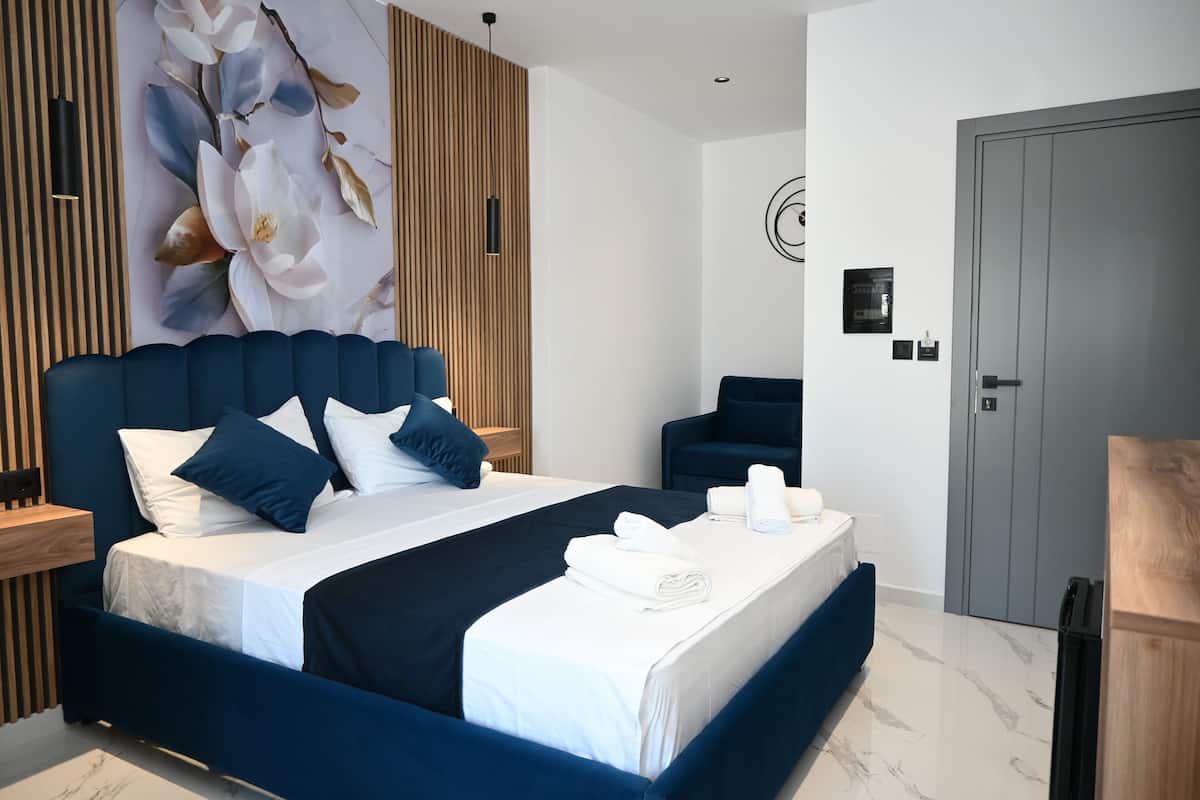 Quarto de hotel moderno com uma cama grande, cabeceira de madeira, uma obra de arte na parede, uma porta cinzenta e uma pequena mesa de madeira.