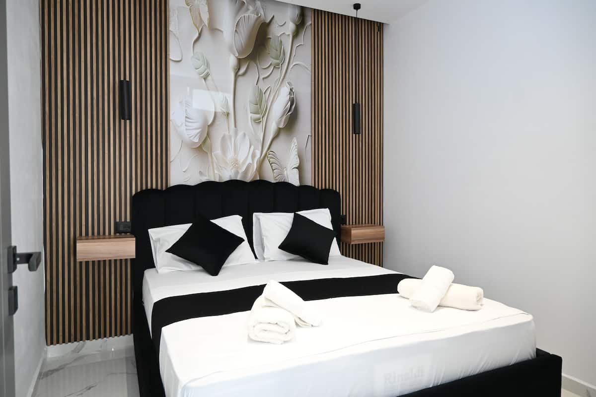 Quarto de hotel moderno com cama grande, roupa de cama preta e branca, parede de painéis de madeira e um painel de parede floral decorativo.