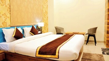 Quarto de hotel com cama grande, duas cadeiras, mesa pequena e mesa de cabeceira.
