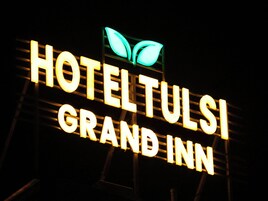 Placa do Hotel Tulsi Grand Inn com letras iluminadas e um logotipo de folha.