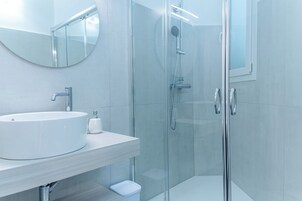 Uma casa de banho moderna com lavatório redondo, cabine de duche em vidro e espelho sobre o lavatório.