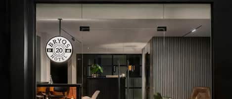 Entrada de hotel moderna, com balcão de recepção, área de estar e restaurante visível ao fundo.