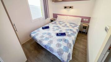 Quarto com cama, janela com cortinas, mesa de cabeceira e prateleira fixada na parede.