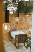 Uma área de refeições com parede de pedra, uma mesa com toalha branca e luminárias pendentes.