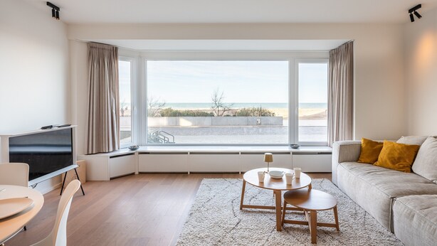 Uma sala de estar moderna com uma janela grande, uma televisão de tela plana, um sofá, uma mesa de jantar e um tapete.