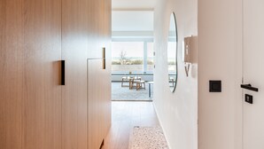 Um corredor moderno com portas de madeira, um espelho grande e vista para uma sala de jantar com área externa.