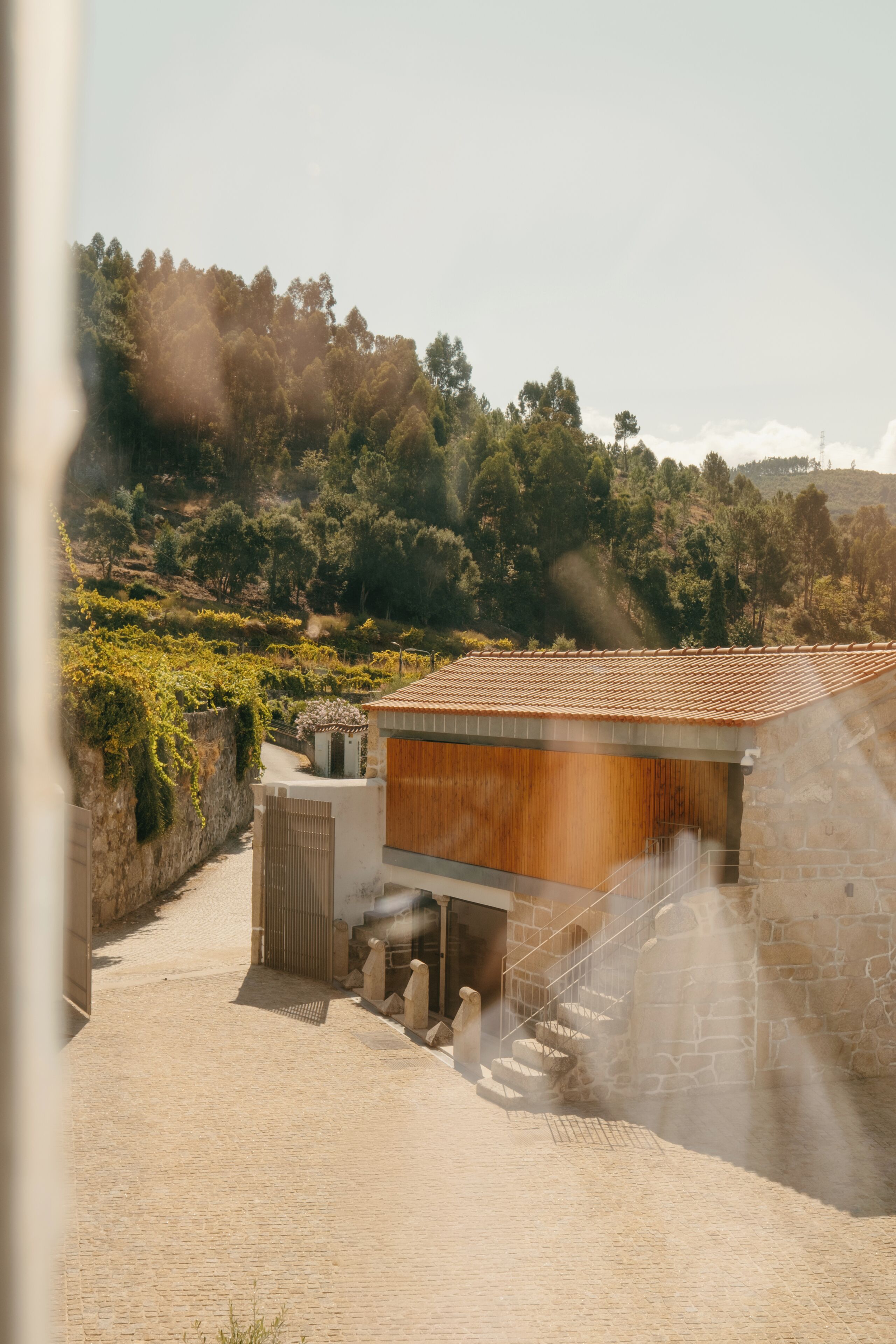 Um edifício com telhado de telhas, parede de pedra e escadaria que leva a uma porta de madeira.