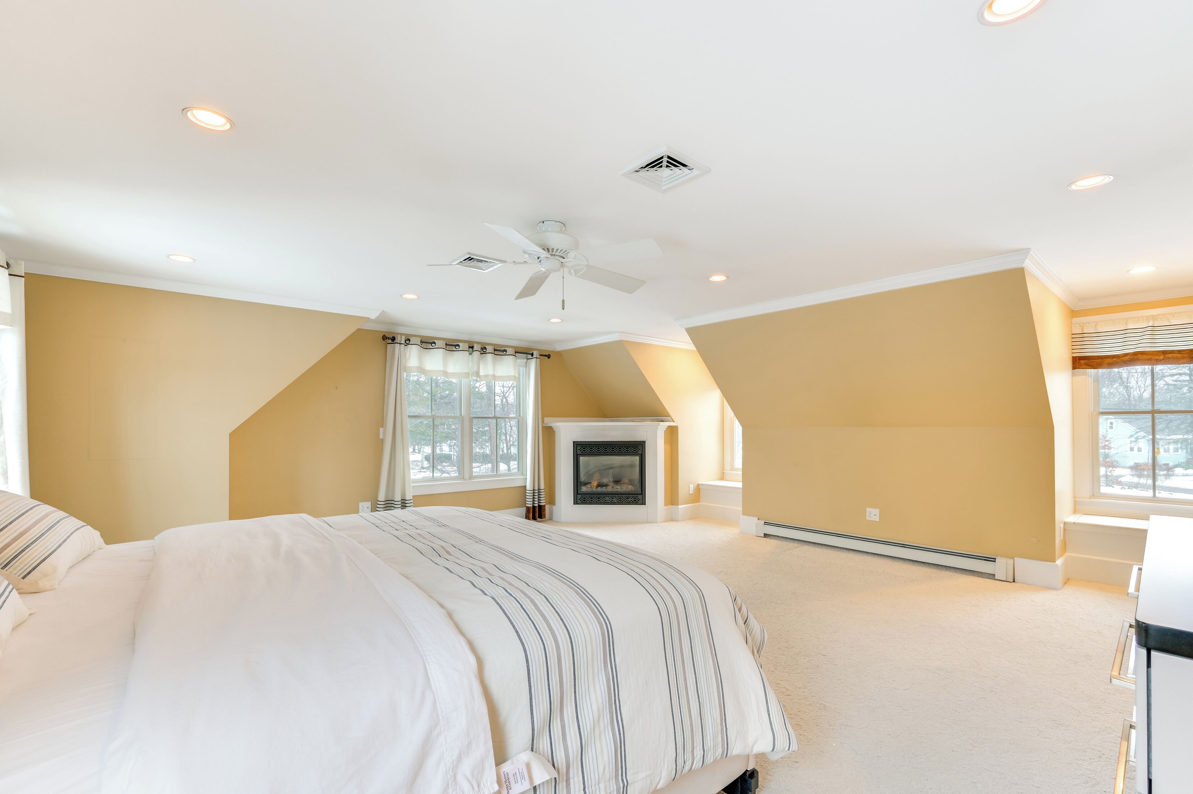 Quarto com cama grande, ventilador de teto, lareira e janela com cortinas.