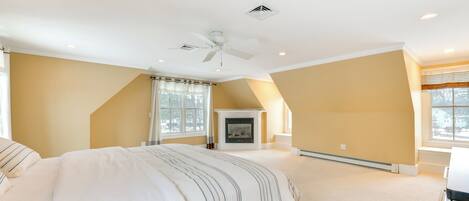 Quarto com cama grande, ventilador de teto, lareira e janela com cortinas.