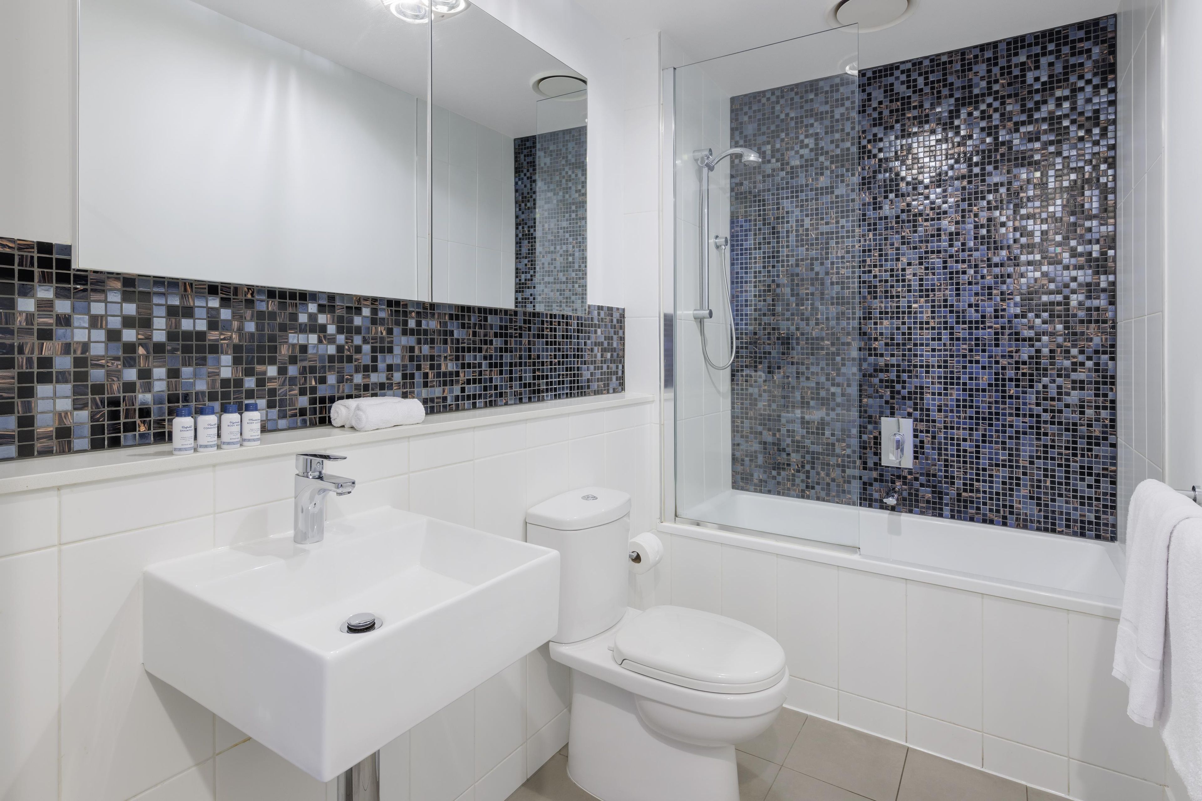 Uma casa de banho moderna com lavatório branco, sanita e chuveiro.