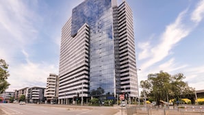 Um edifício moderno de arranha-céu com fachada de vidro refletivo, vários andares e uma entrada de canto imponente.