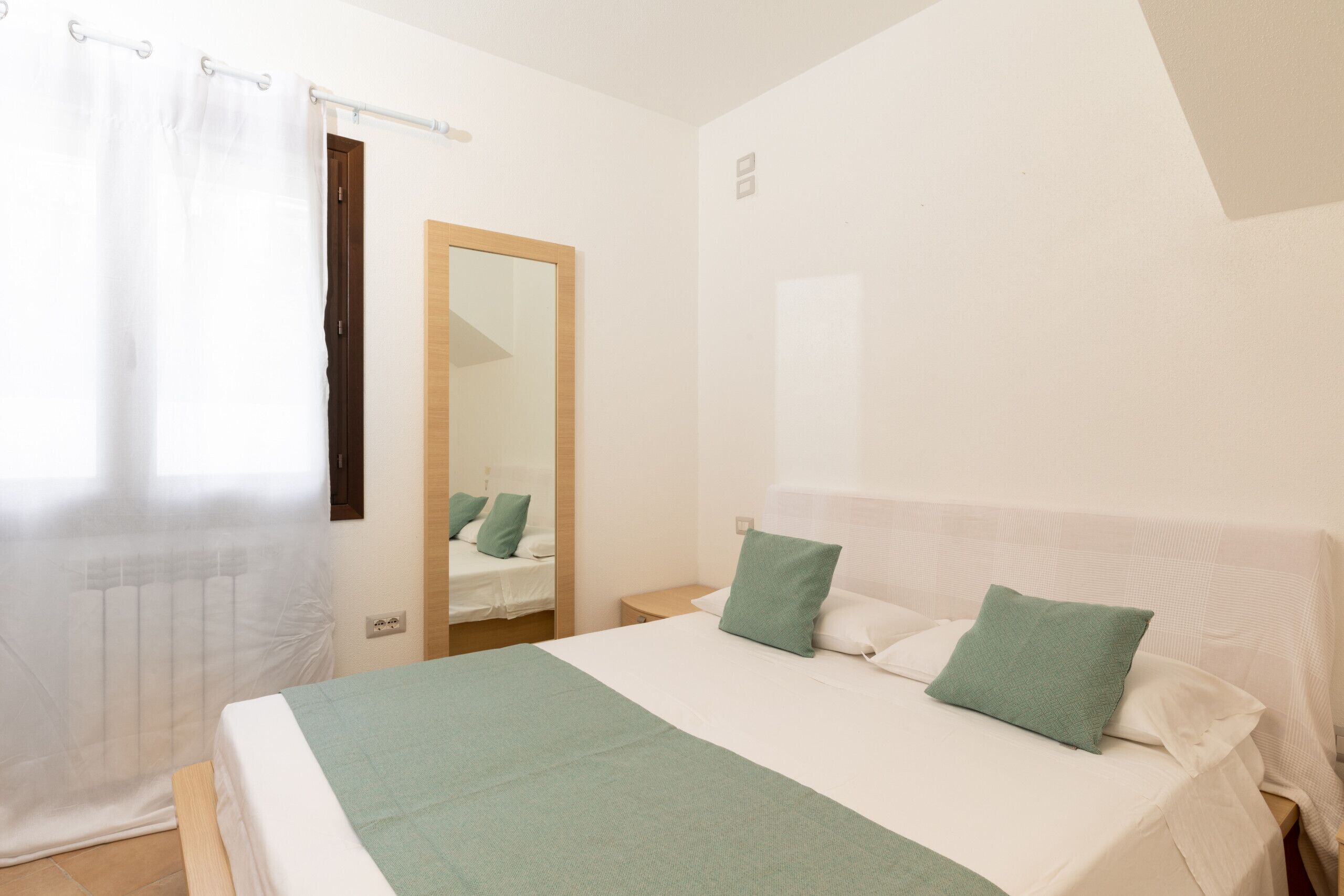 Quarto com cama, espelho, porta de madeira e cortina.