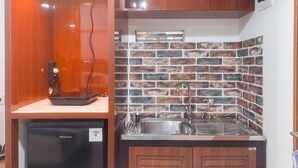 Uma cozinha compacta com painel de backsplash de tijolos, uma pia e um refrigerador pequeno.