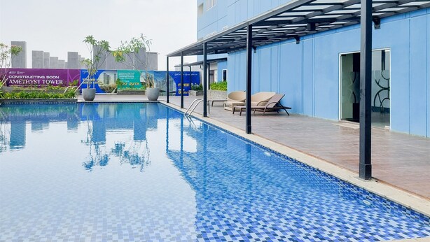 Piscina com piso de azulejos, área de estar coberta e um edifício com fachada azul.
