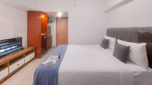 Quarto de hotel com uma cama, uma televisão sobre um suporte de madeira e uma porta que dá para um banheiro.