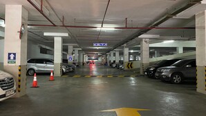 Garagem de estacionamento com vários níveis, carros estacionados em ambos os lados e placas de sinalização indicando as áreas de estacionamento.