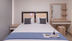 Quarto de hotel com cama, mesas de cabeceira, espelho e pequena escrivaninha de madeira.