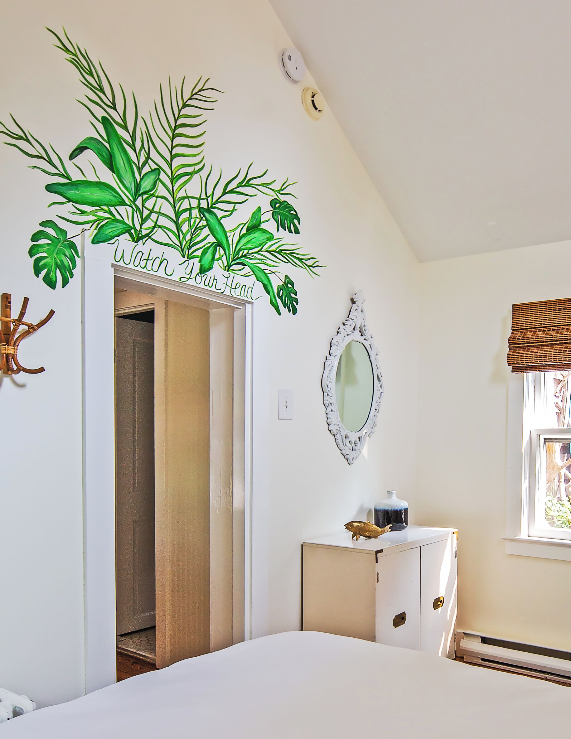 Quarto com cama, penteadeira, espelho e porta que dá para outro cômodo.