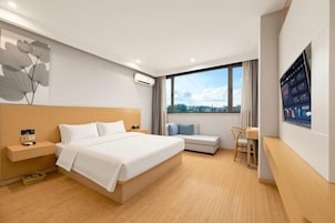 Quarto de hotel moderno com uma cama grande, área de estar, escrivaninha e vista para a cidade.