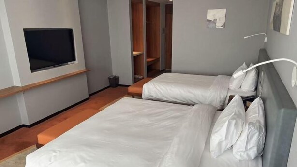 Quarto de hotel com duas camas, televisão presa na parede, chão de madeira e um armário com portas deslizantes.