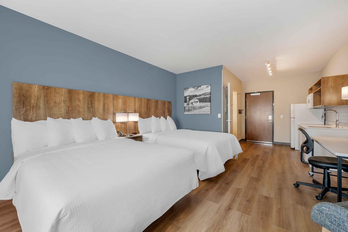Quarto de hotel com duas camas, cozinha compacta e banheiro.
