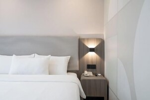 Quarto de hotel com uma cama, mesa de cabeceira com telefone e luminária na parede.