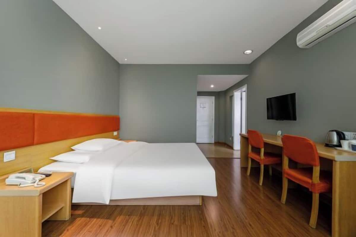Quarto de hotel com cama, mesa de cabeceira, escrivaninha, cadeiras e televisão.