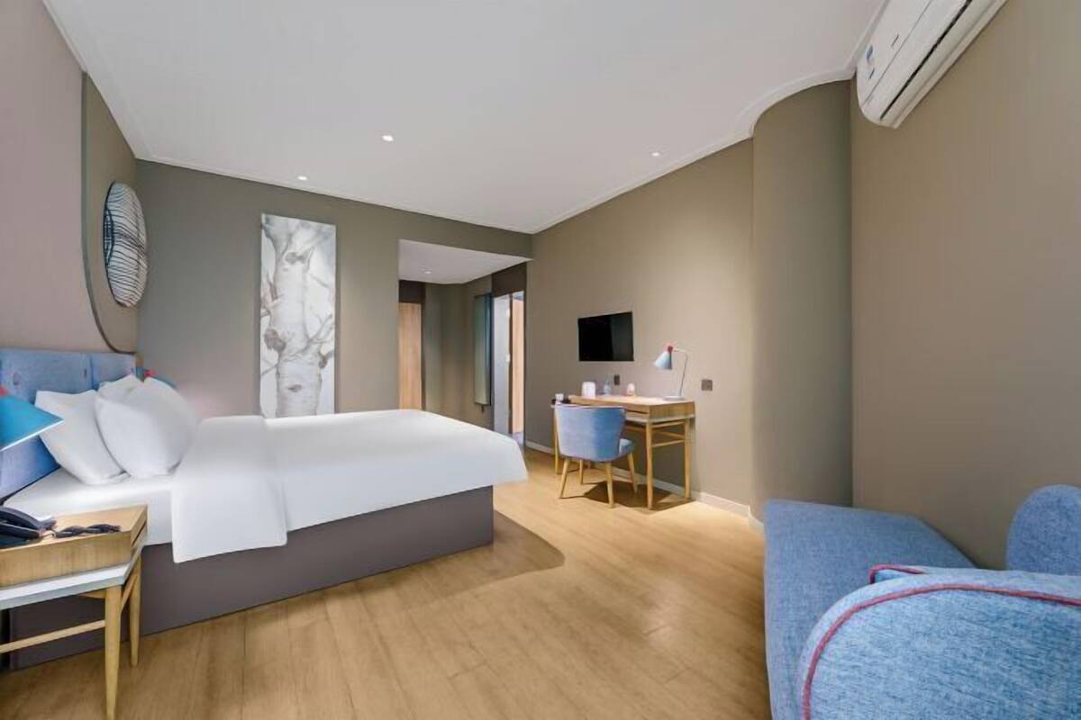 Quarto de hotel moderno com uma cama grande, uma escrivaninha, uma cadeira e uma televisão.