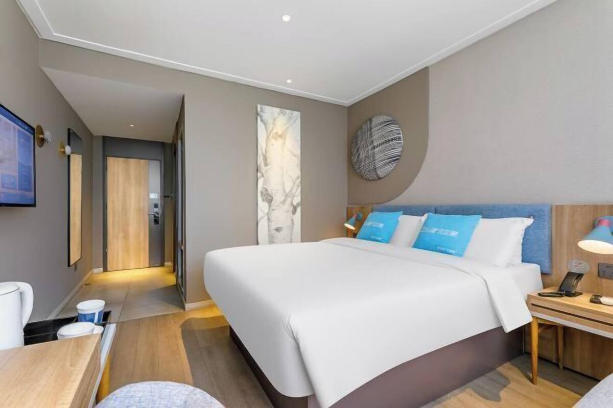 Quarto de hotel moderno com uma cama grande, mesas de cabeceira, uma escrivaninha e vista para o corredor.